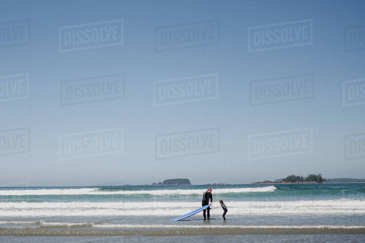 Father and child surfing on beach, Tofino, Canada - Stock Photo - Dissolve