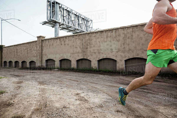 Young male runner running on urban wasteland, neck down - Stock Photo ...