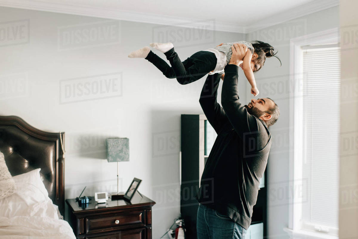 Girl being held up by father in bedroom - Stock Photo - Dissolve