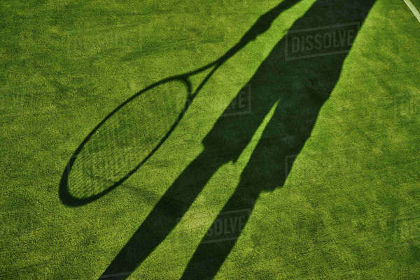 Cropped shadow of tennis player with tennis racket on green lawn ...