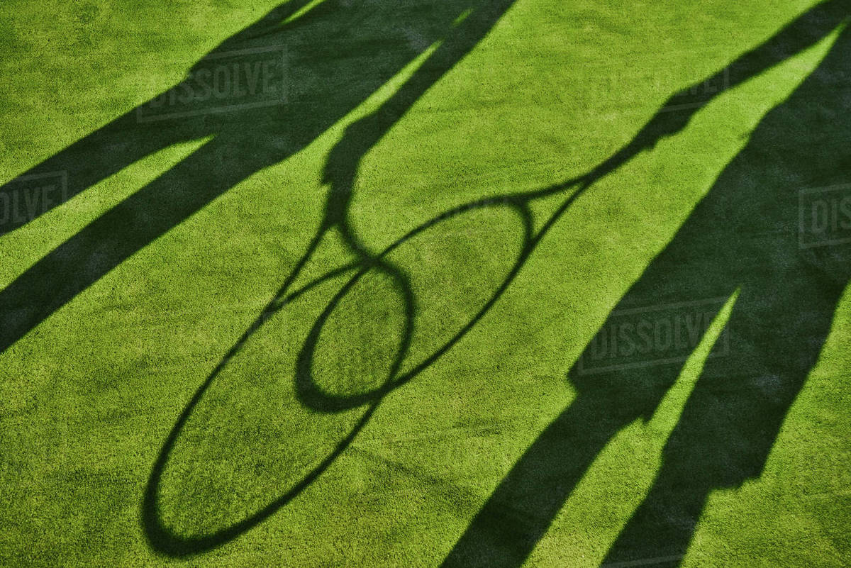 Cropped shadows of two tennis players with tennis rackets on green lawn ...