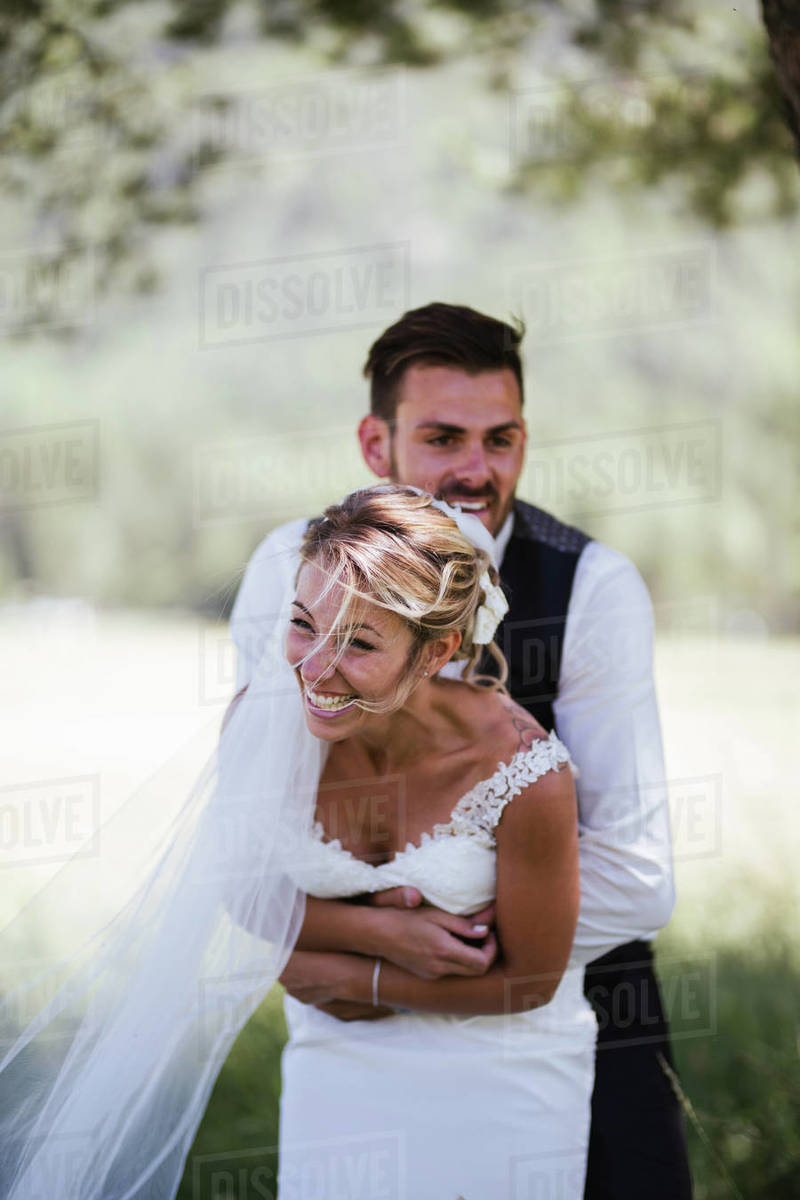 Romantic groom hugging bride from behind in woodland - Royalty-free ...