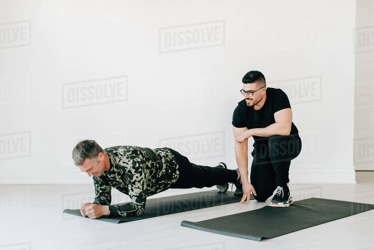 Fitness instructor observing man doing plank in studio - Royalty-free ...