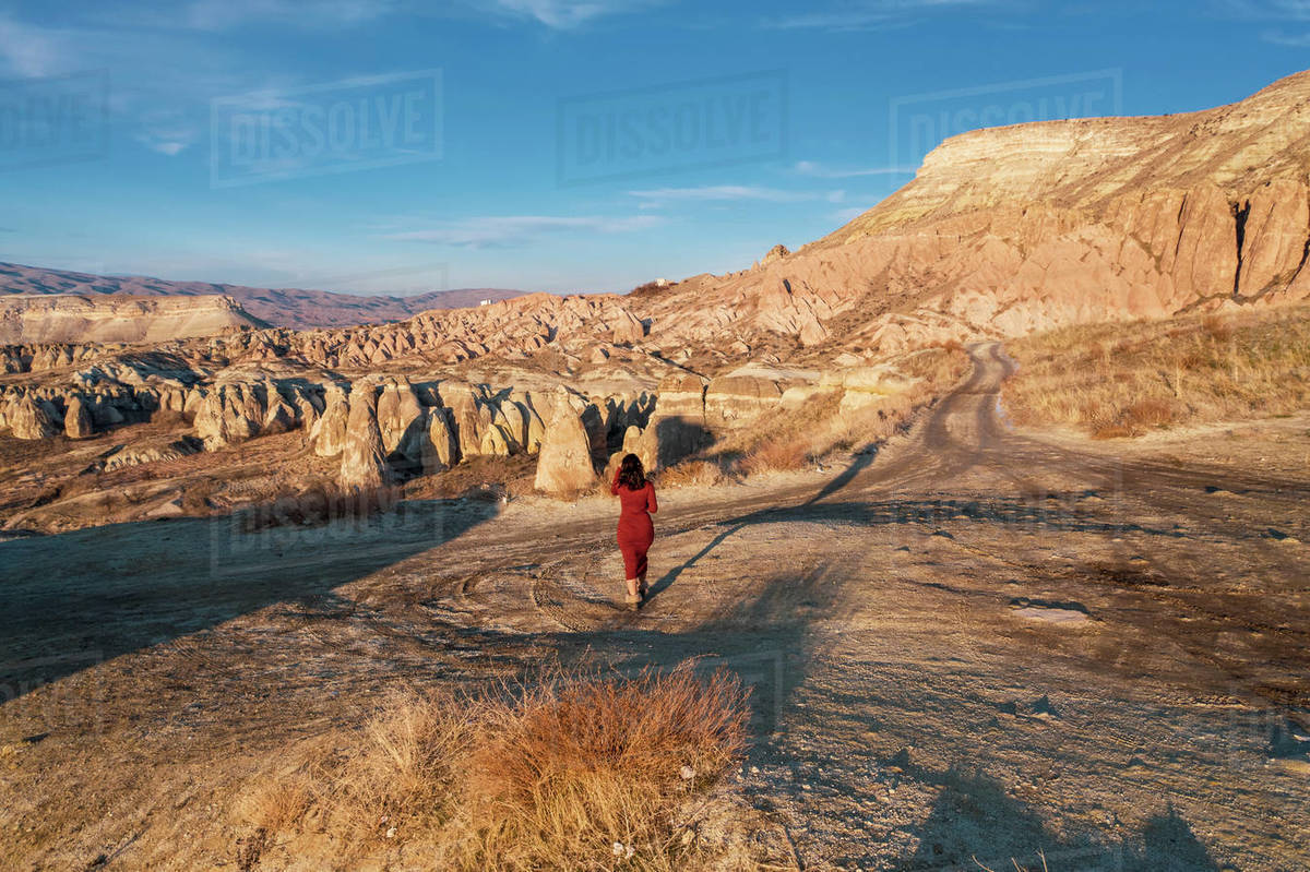 Turkey, Cappadocia, Rear view of woman in red dress walking in rocky ...