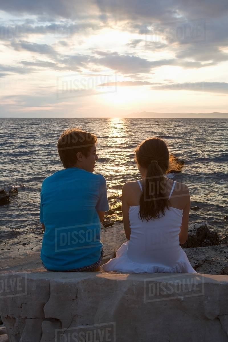 Teenage couple watching sunset over sea - Stock Photo - Dissolve