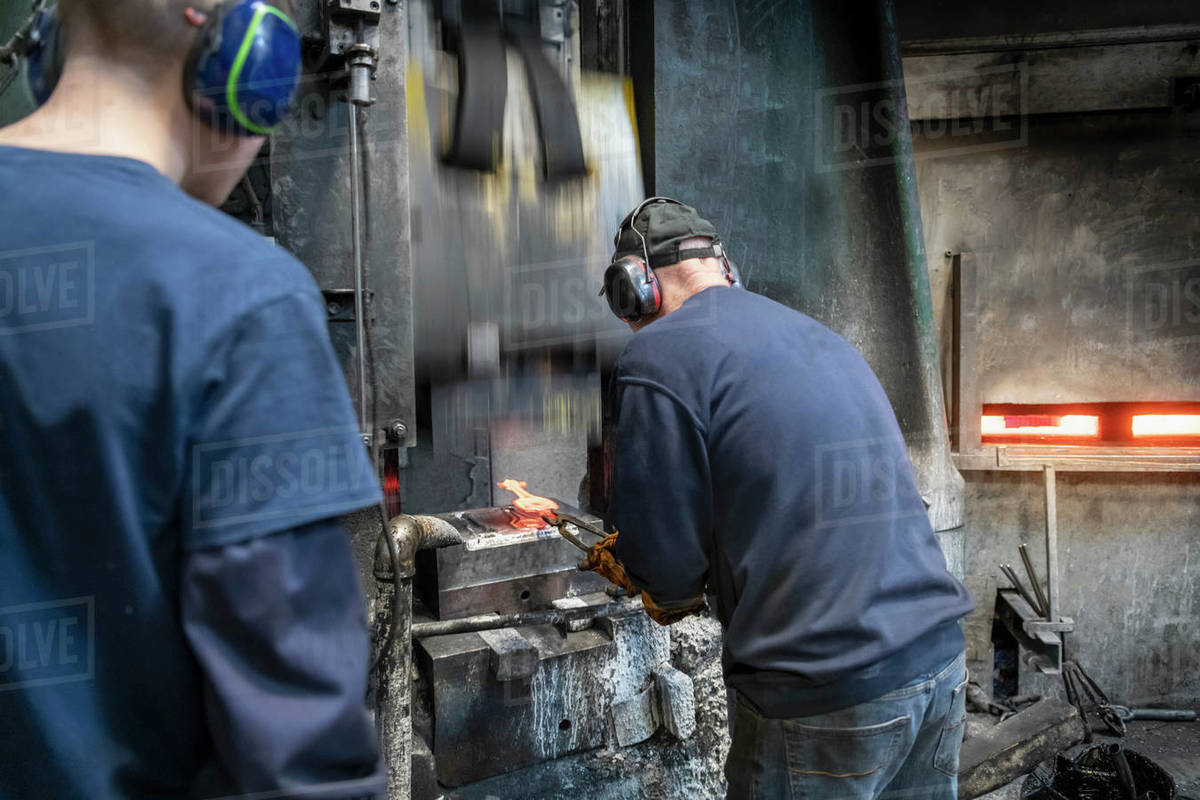 Engineer with apprentice forging steel parts in hammer press in ...