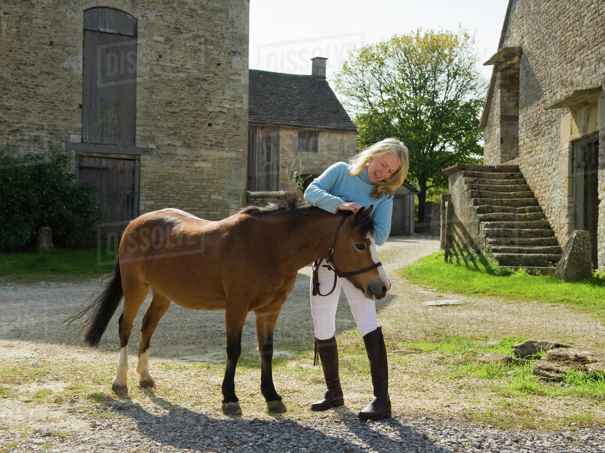 Smiling woman attending pony at farm - Royalty-free Stock Photo | Dissolve