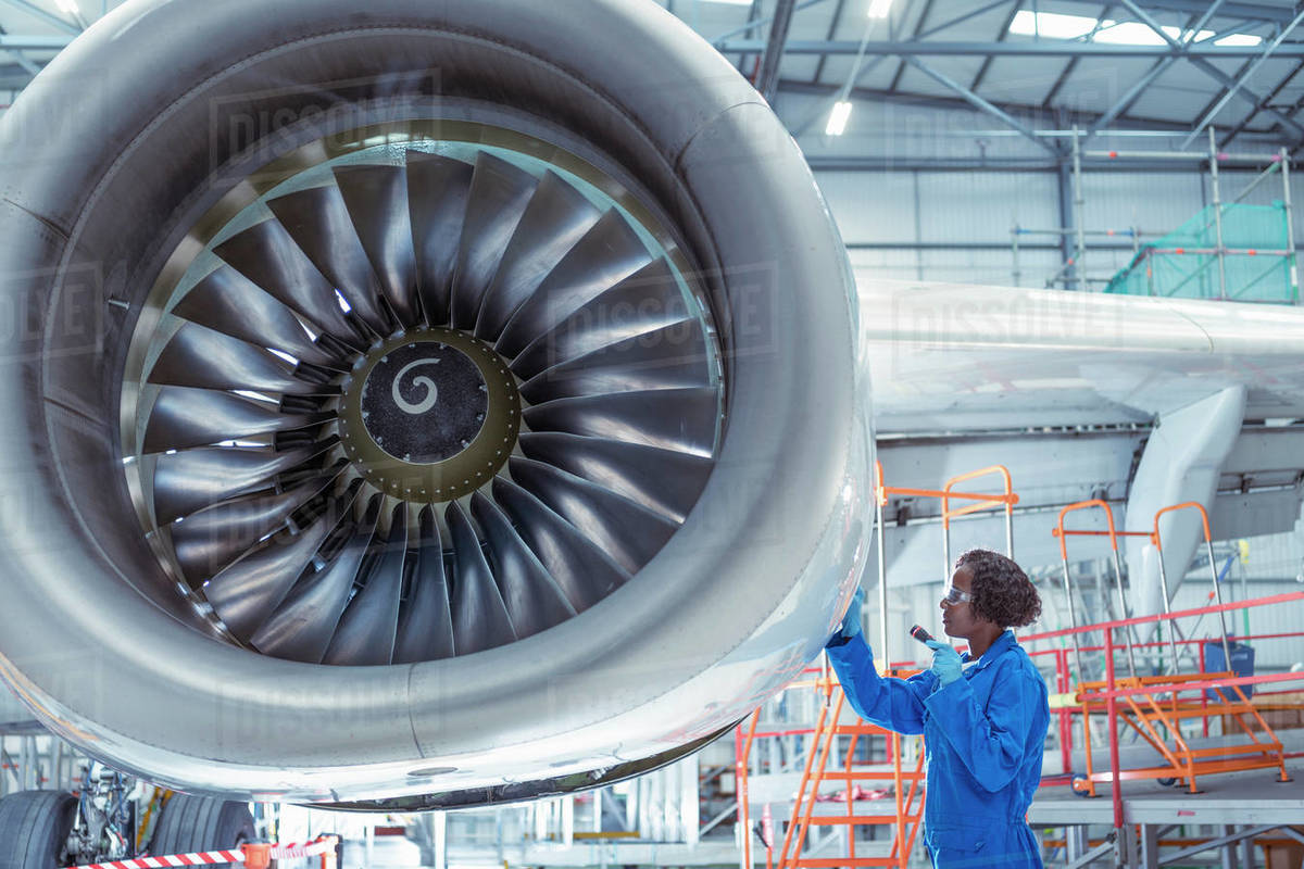 Female aircraft maintenance engineer inspecting large jet engine in ...