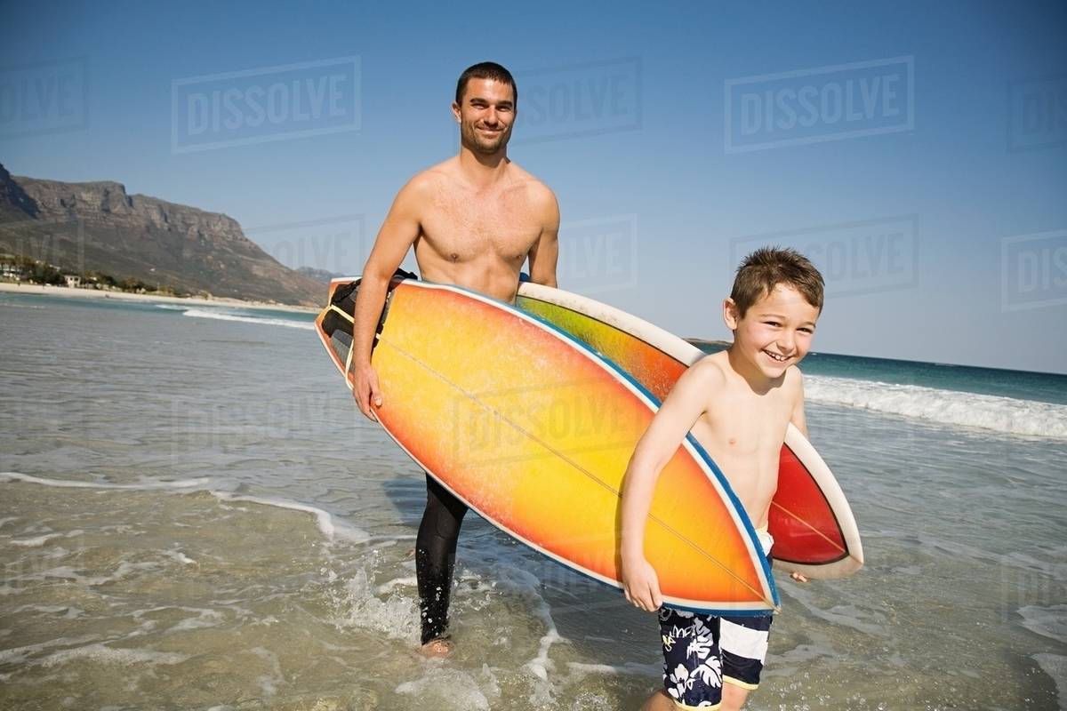 Father and son carrying surfboards in from the sea - Royalty-free Stock ...