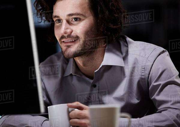 Young man looking at computer monitor, working late - Royalty-free ...