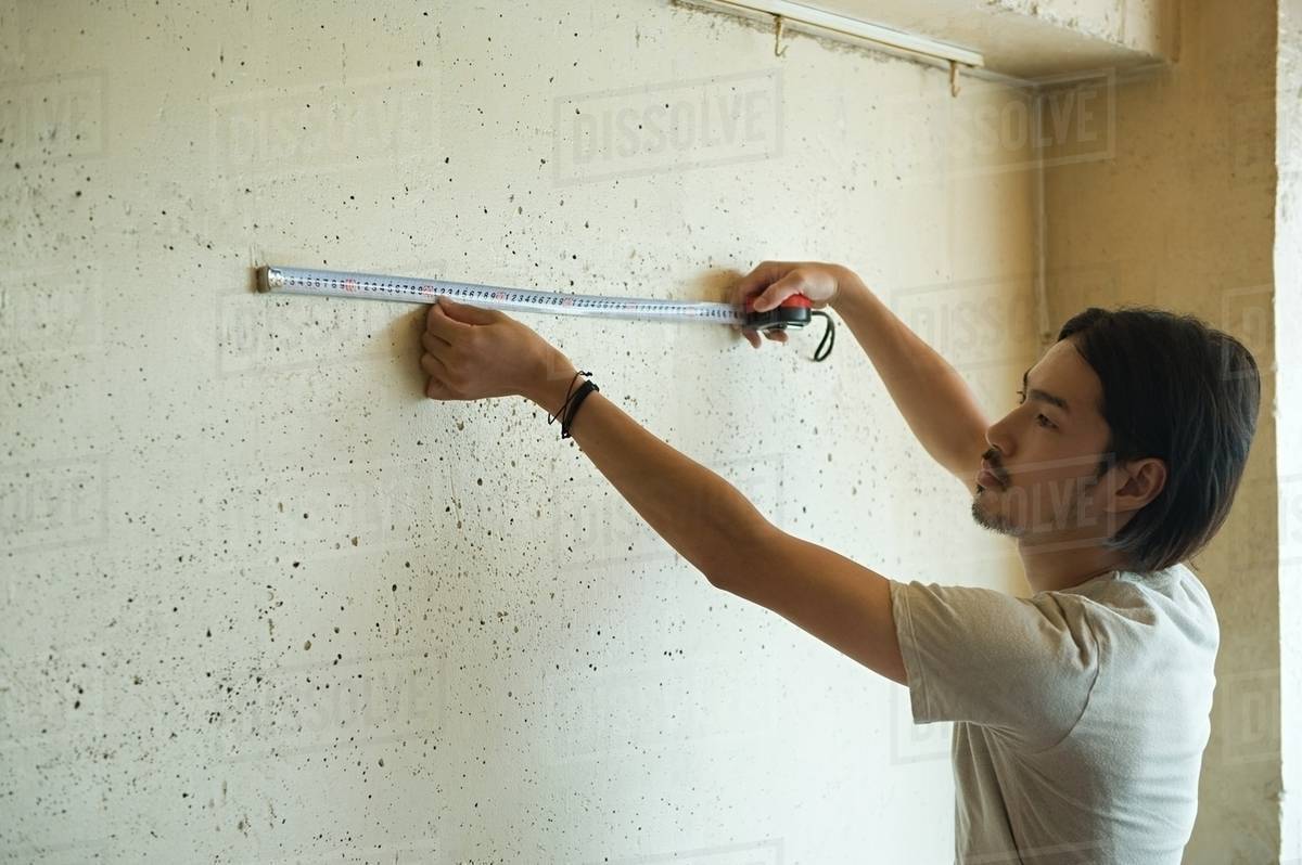 Young man measuring wall - Royalty-free Stock Photo | Dissolve