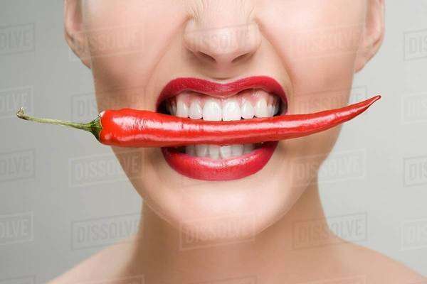 Woman with a red chili pepper between her teeth - Stock Photo - Dissolve