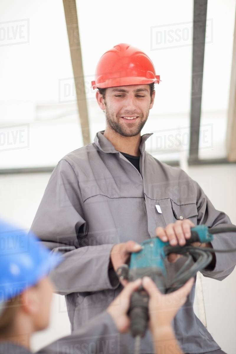 Male and female laborer handing electric drill on construction site ...