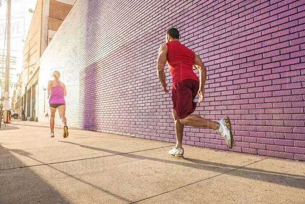 Rear view of male and female runners running along sidewalk - Stock ...