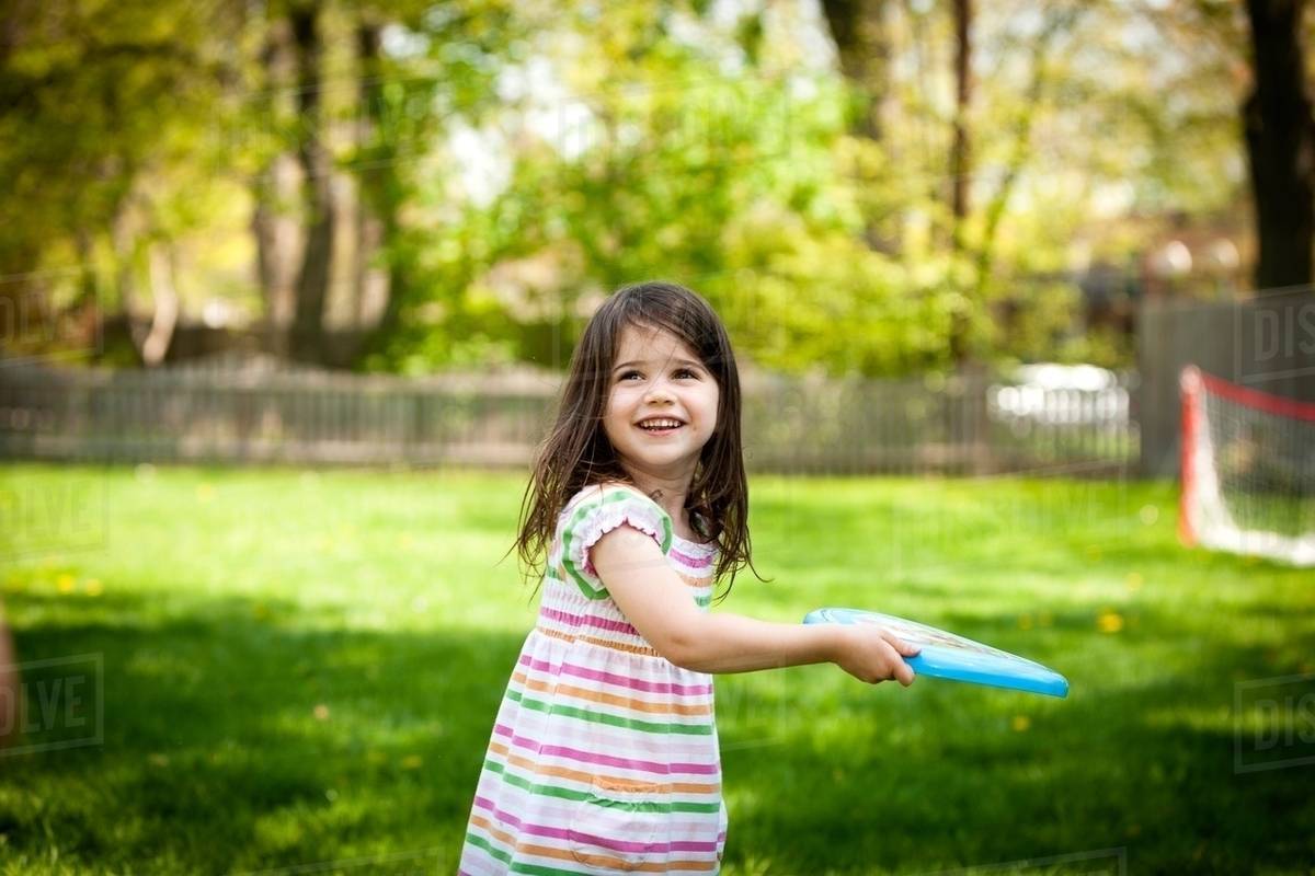 Young girl throwing frisbee in garden - Royalty-free Stock Photo | Dissolve