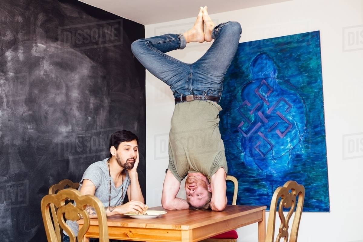 Male couple at home, young man eating meal whilst his partner does ...