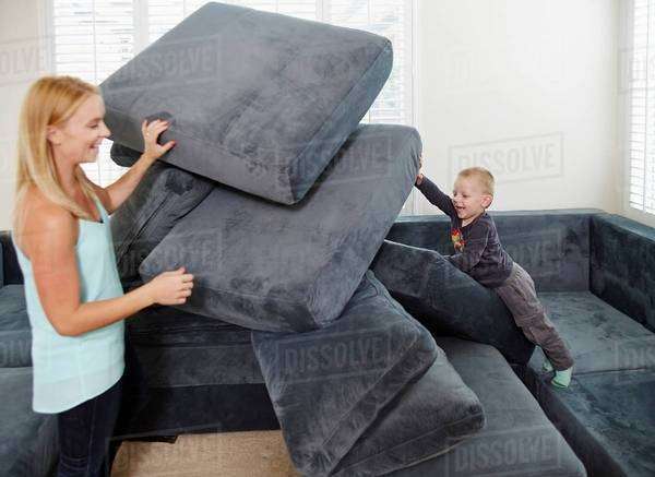 Boy pushing over cushions in living room - Stock Photo - Dissolve