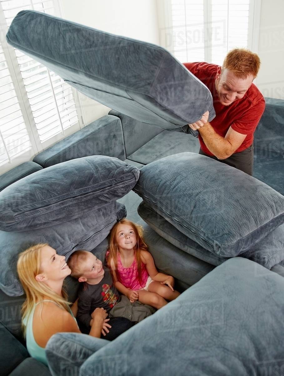 Father covering family sitting among cushions in living room - Royalty ...