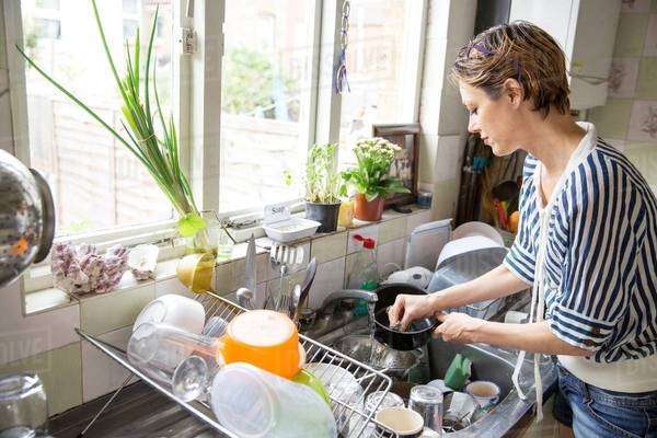 Mid adult woman washing up at kitchen sink - Stock Photo - Dissolve