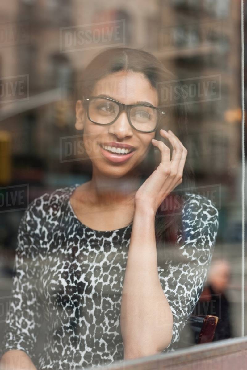 Woman looking out of window talking on cell phone - Stock Photo - Dissolve