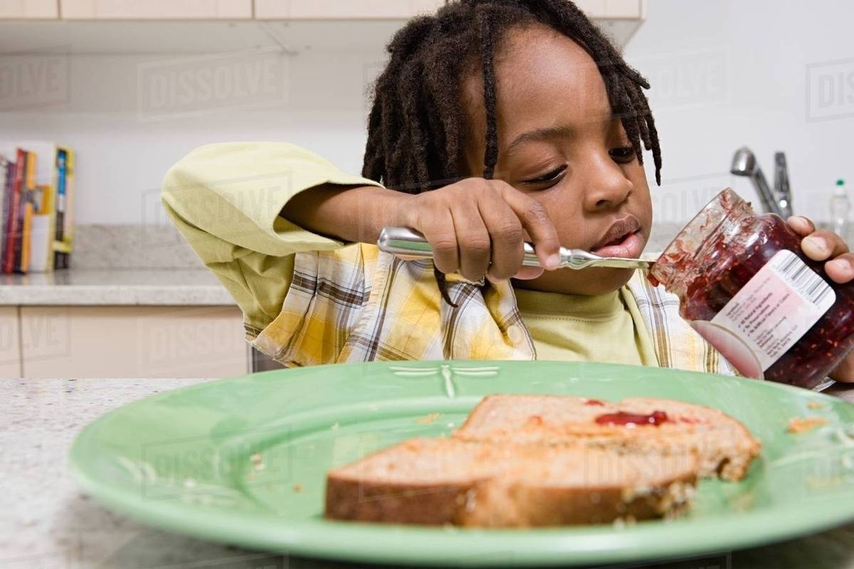 Boy scooping jam out of jar - Stock Photo - Dissolve