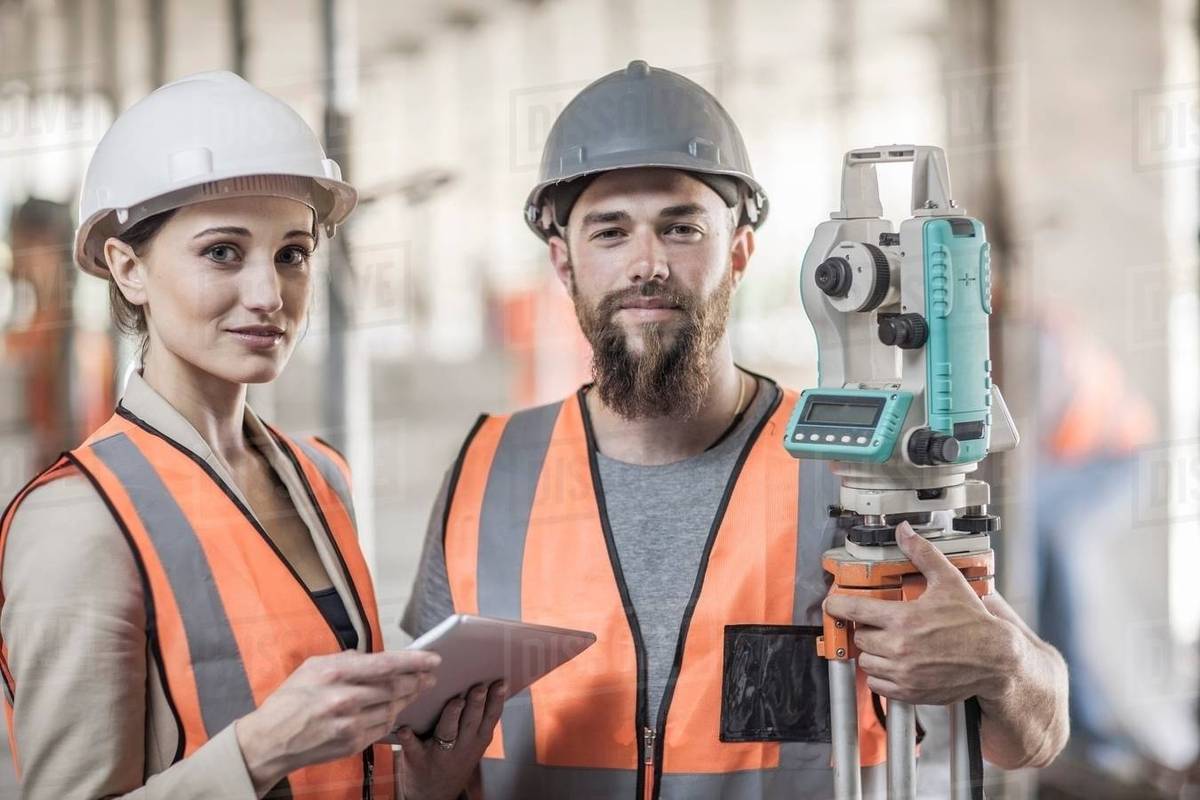 Portrait of young male and female surveyors on construction site ...