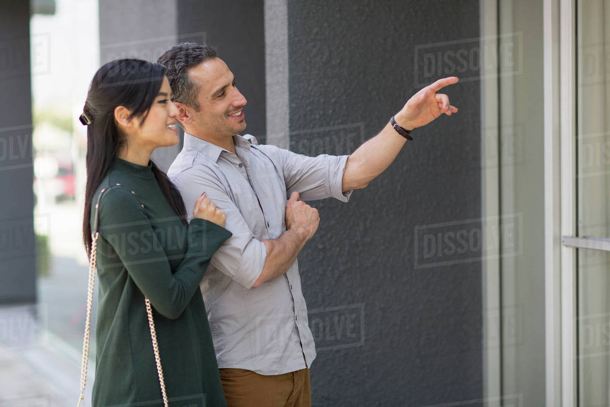 Couple window shopping pointing and smiling - Stock Photo - Dissolve