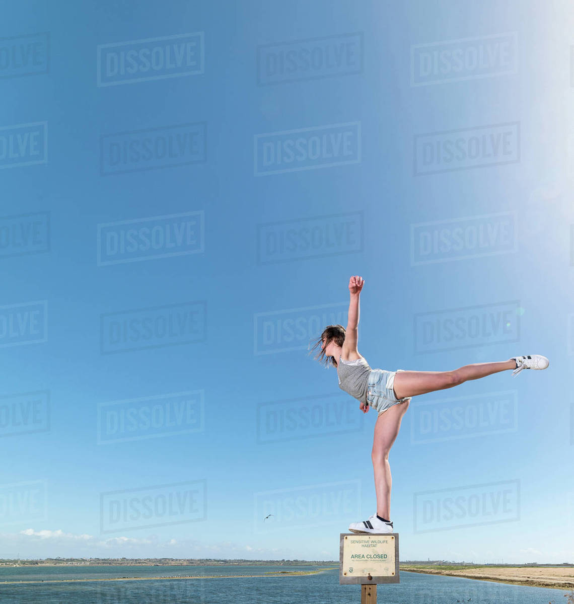 Girl balancing on beach signage - Royalty-free Stock Photo | Dissolve