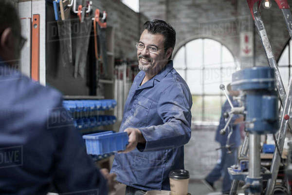 Worker handing over tray in workshop - Royalty-free Stock Photo | Dissolve