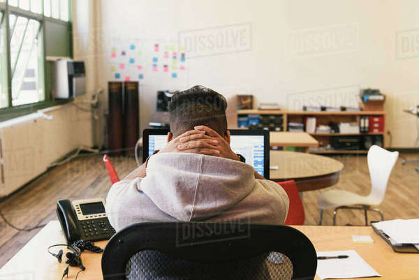Rear view of man at desk in office, hands behind neck - Stock Photo ...