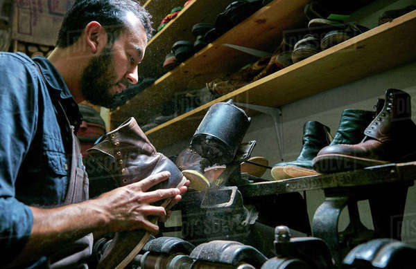 Male cobbler in traditional shoe workshop repairing boot heel - Royalty ...