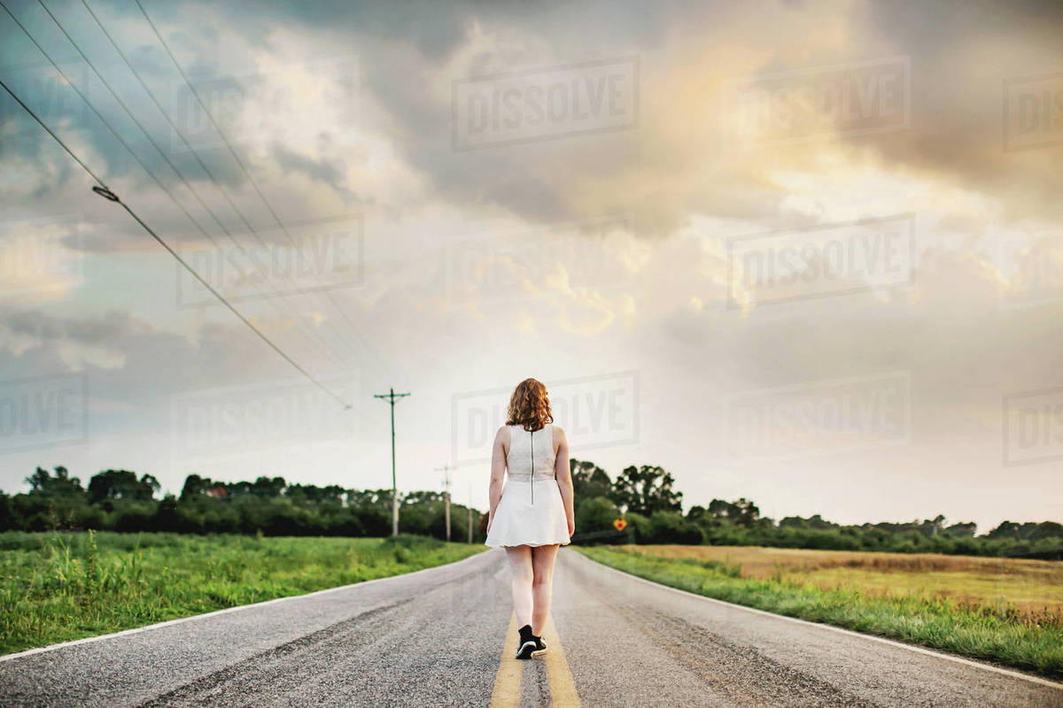 Rear view of woman walking down centre of rural road - Stock Photo ...