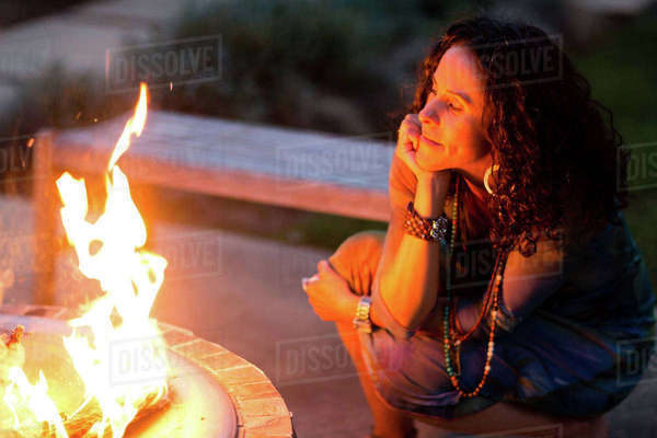 Mature woman crouching and watching patio fire at dusk - Royalty-free ...