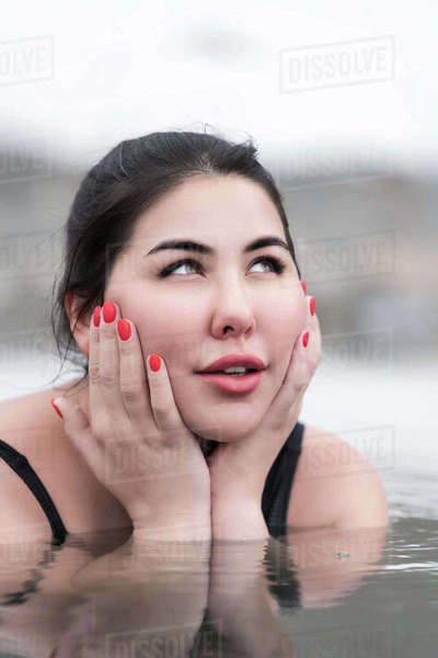 Woman embracing face with her palms, playfully looking up. Portrait of ...