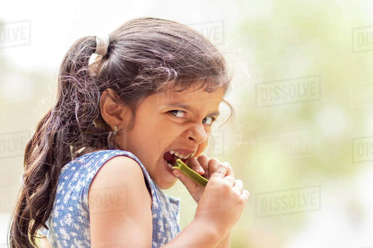 Little girl biting a fruit in the field - Stock Photo - Dissolve