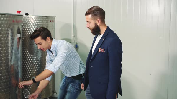 Men tasting fresh wine during production. Young men trying white wine ...