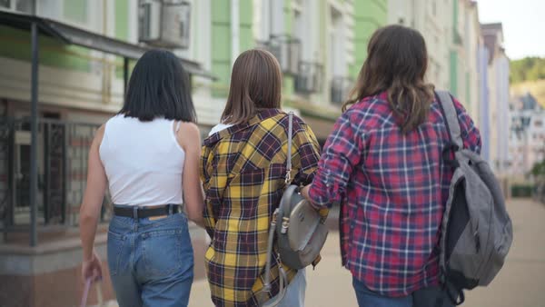 Back view happy girlfriends strolling on city street holding hands ...