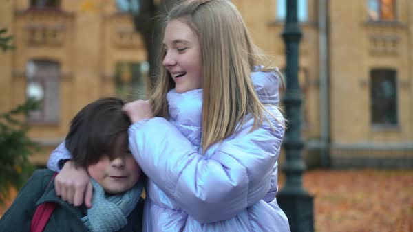 Teenage girl rubbing hair of cute little boy bullying standing outdoors ...