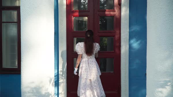 Back view slim curious lady in vintage dress walking to door opening ...