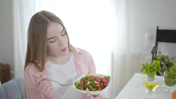 Portrait of happy Caucasian woman eating fresh spring salad of tomatoes ...