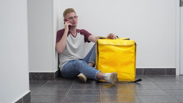 Wide shot positive male courier sitting on floor in business center ...