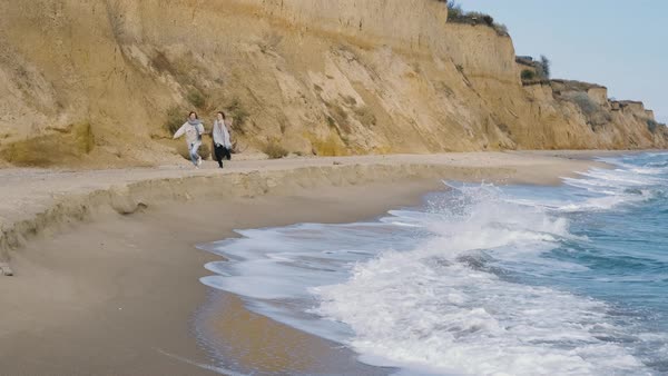 Woman couple run holding hands along the sea beach. Two girls running ...