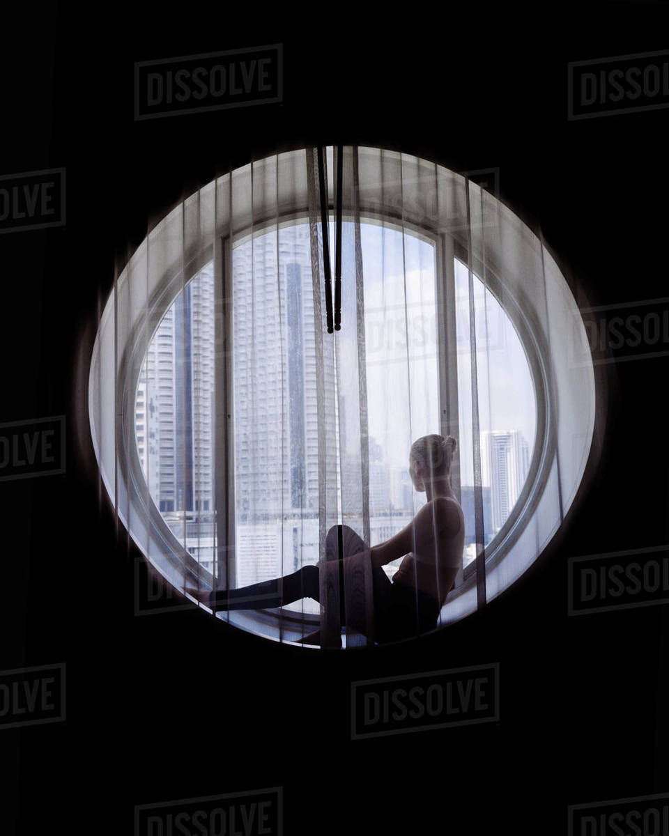 Silhouette of woman sitting in the round window - Stock Photo - Dissolve