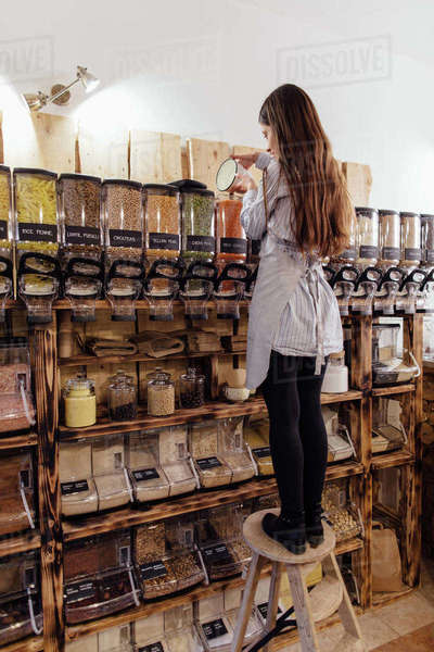 Shopkeeper working in zero waste shop. Shop assistant filling glass jar ...