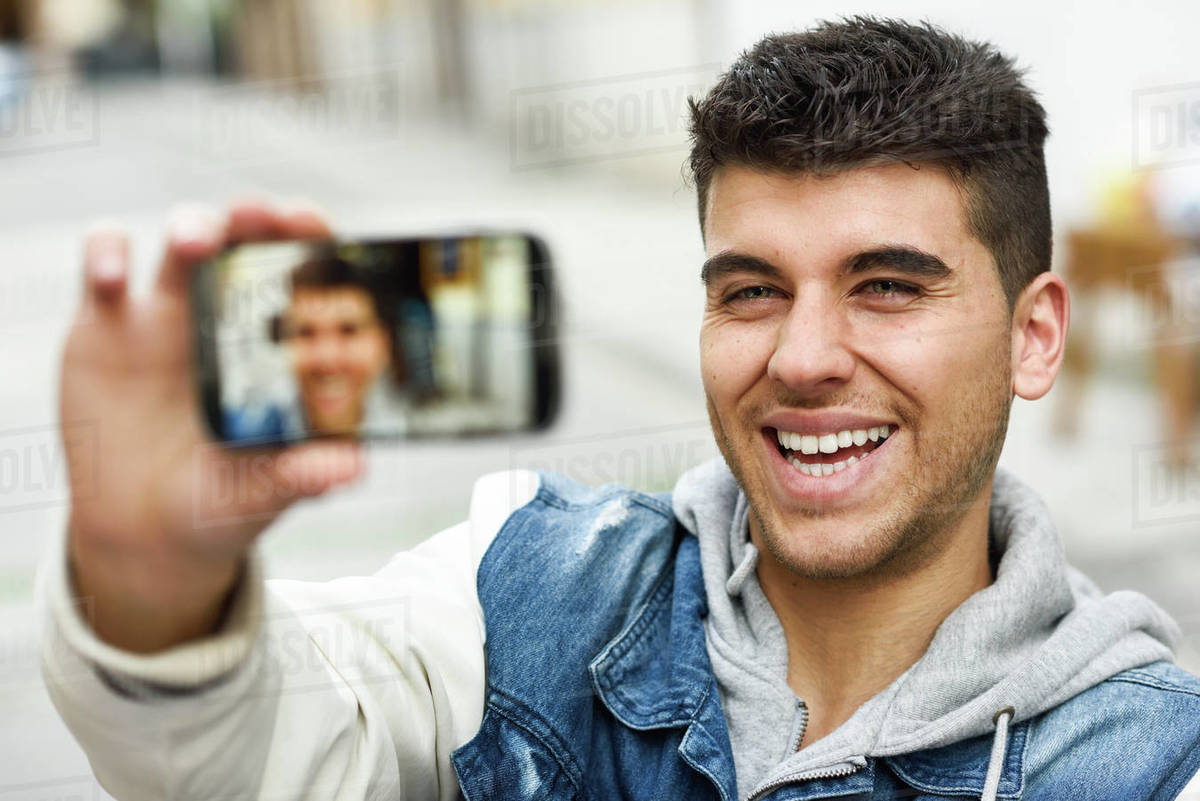 Handsome young man selfie in urban background with a smartphone wearing ...