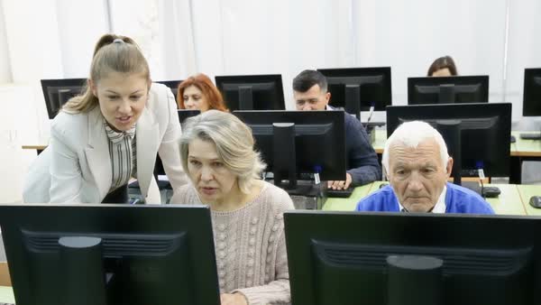 Elderly people working on computers with young female teacher while ...