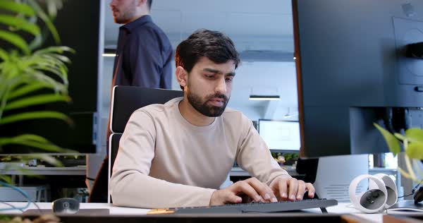 Handsome Arab man sitting at computer screen and typing on keyboard ...