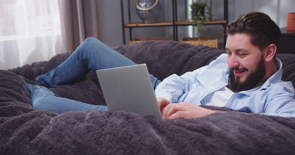 Close up right angle shot of adult man lying on sofa typing on laptop ...