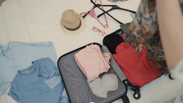Woman packing up her summer clothes into suitcase and leaving the house ...