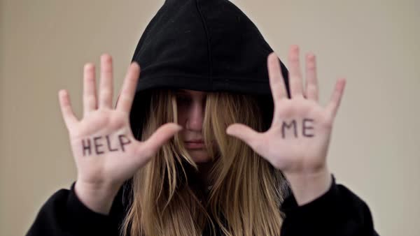 Teenage girl, covering her face with a hood, shows her palms with the ...